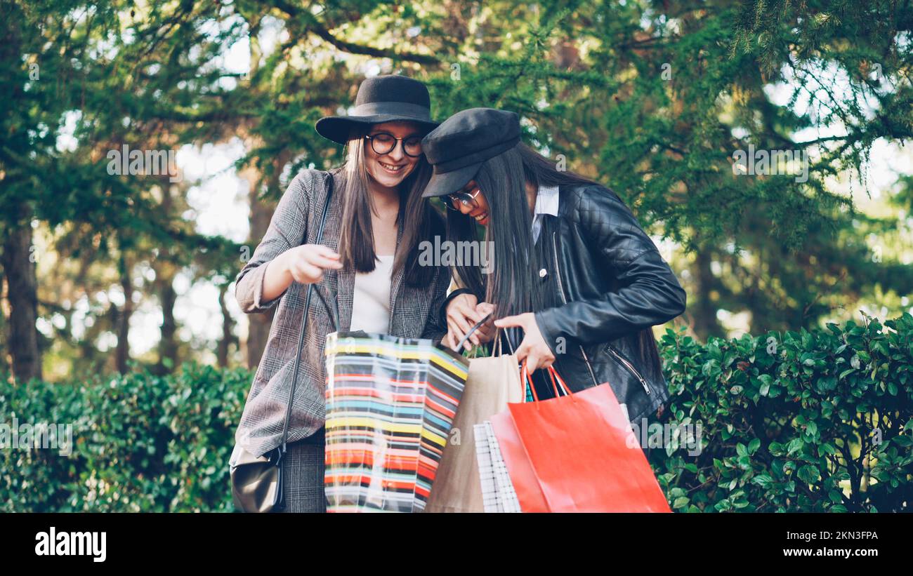 Two young women shopaholics are talking in the street in city looking ...