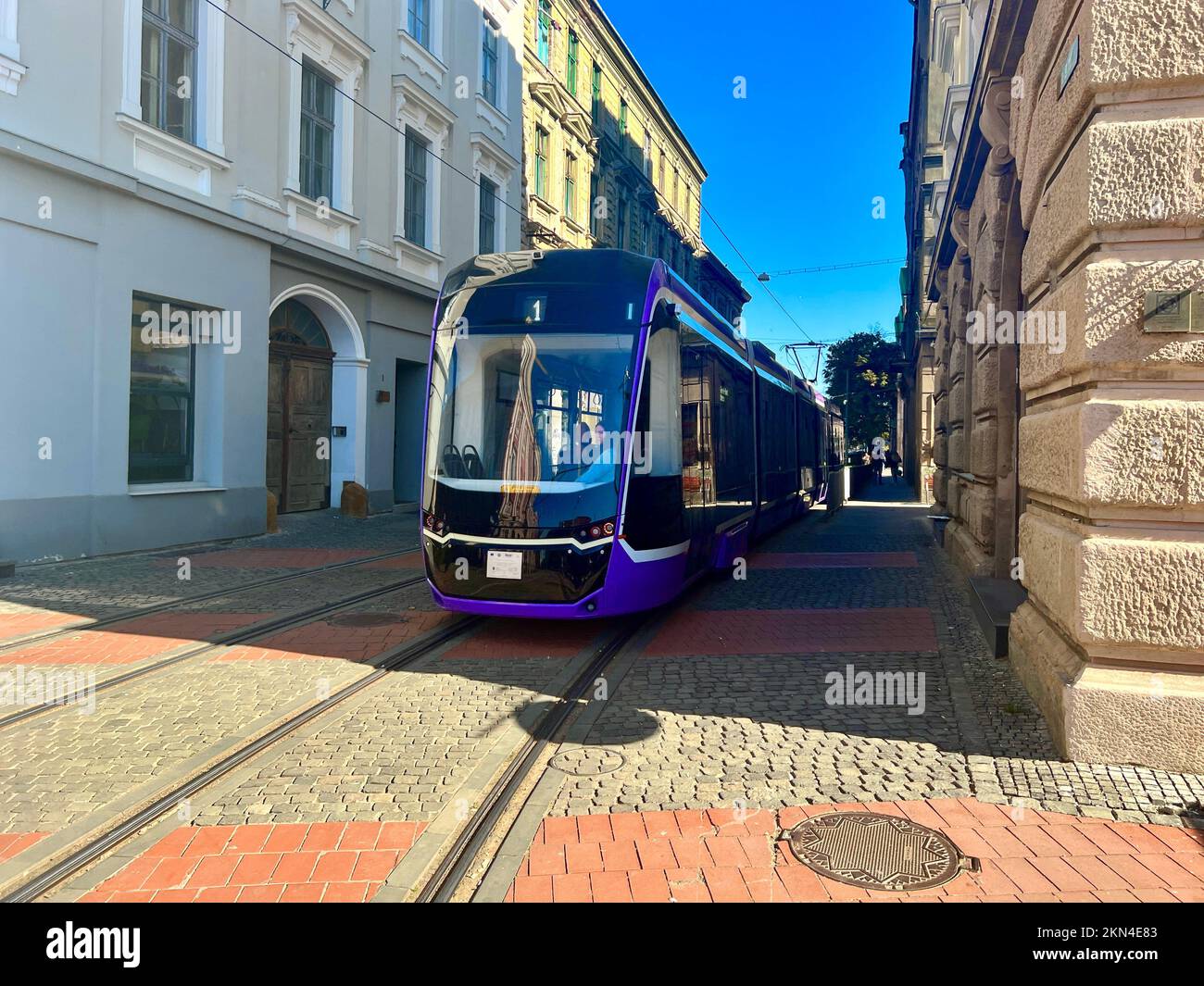 A purple public tram in Timisoara, Romania, in sunny weather surrounded ...