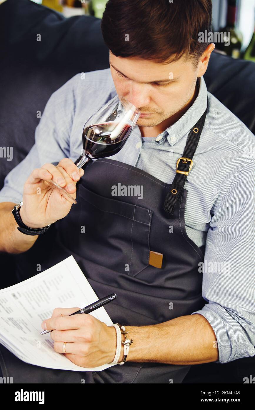 Male sommelier tasting red wine and making notes. Profession in ...