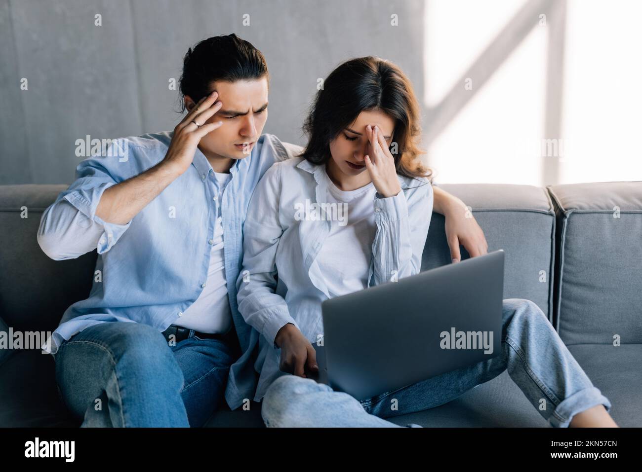 Confused upset millennial married couple sit on couch read financial ...