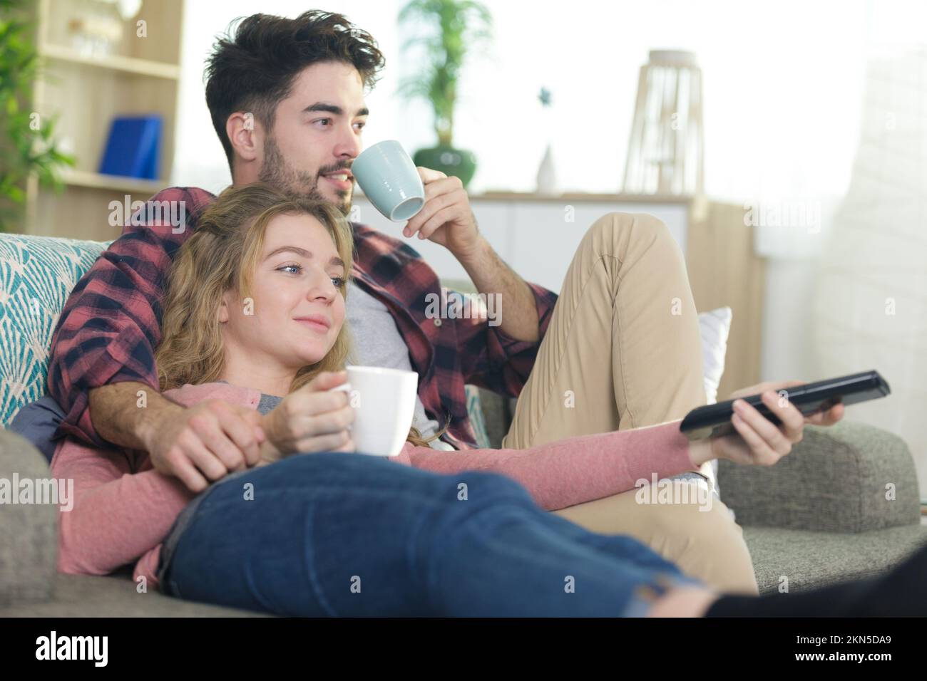 couple snuggling on sofa with cup of tea watching tv Stock Photo - Alamy