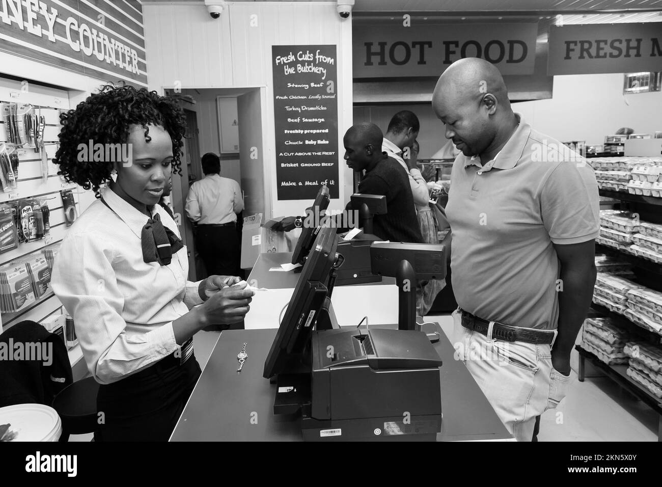A grayscale shot of an African cashier and customer at checkout at a ...