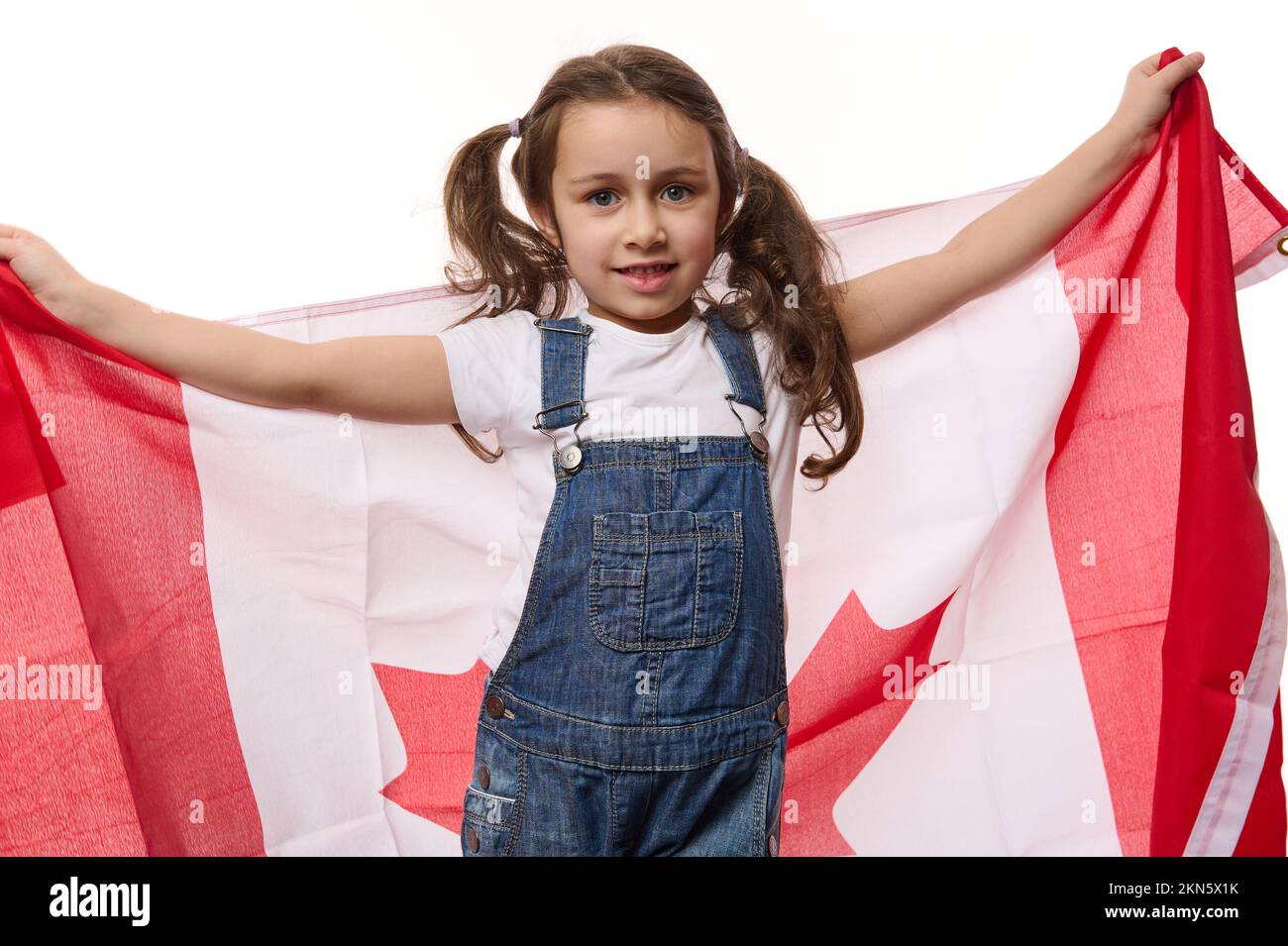 Happy little girl in denim overalls, carries Canadian flag on Canada ...