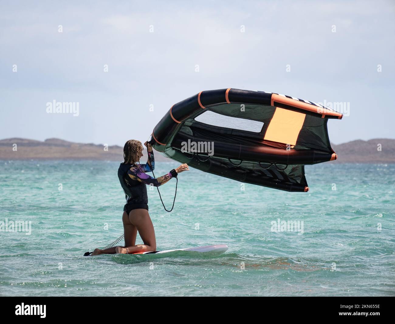 Young woman in the ocean holding wingfoil wing after falling practicing ...