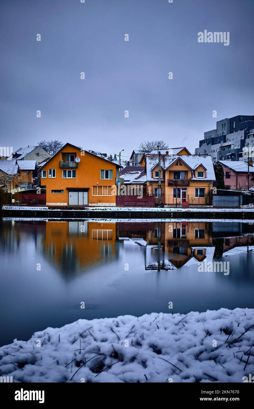A vertical shot of colorful houses reflecting on a frozen lake in Cluj ...