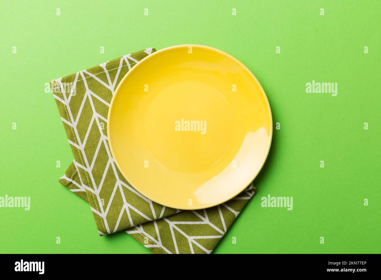 Top view on colored background empty round yellow plate on tablecloth ...