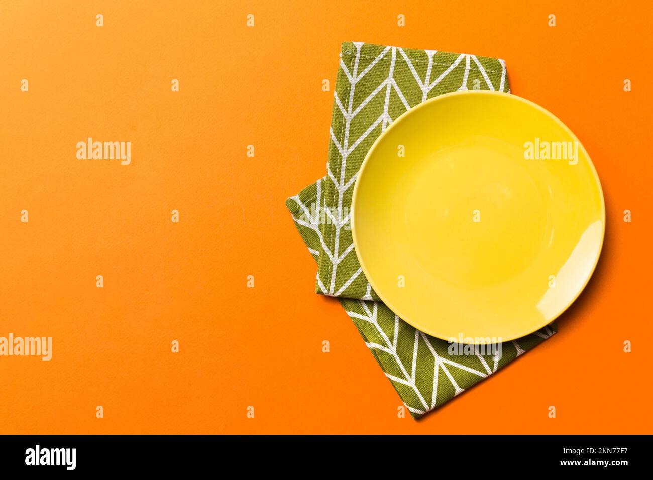Top view on colored background empty round yellow plate on tablecloth ...