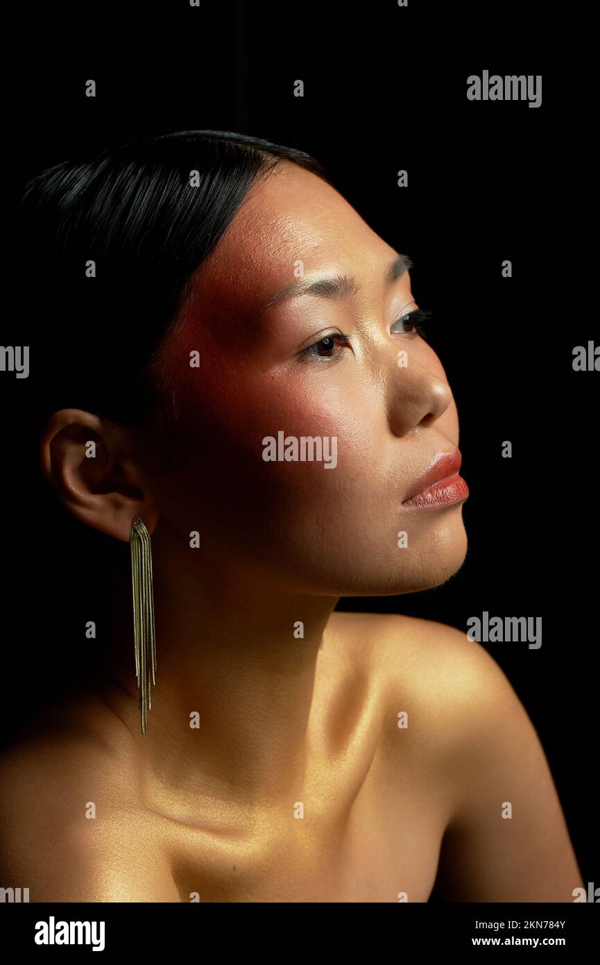 An Asian girl with golden skin looks in profile. Long gold earrings ...
