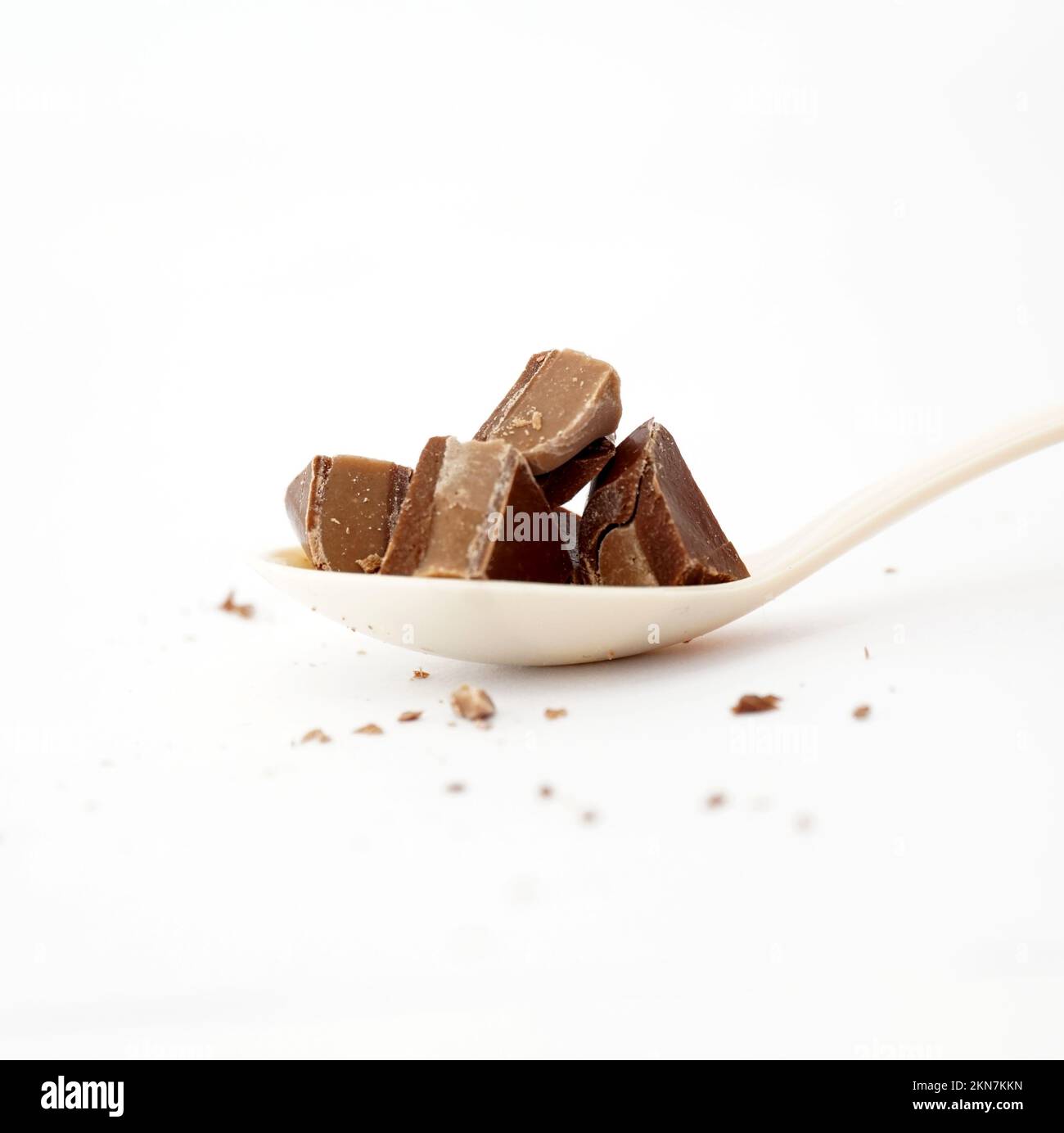 Chocolate bar. Broken pieces in small plastic spoon over white ...