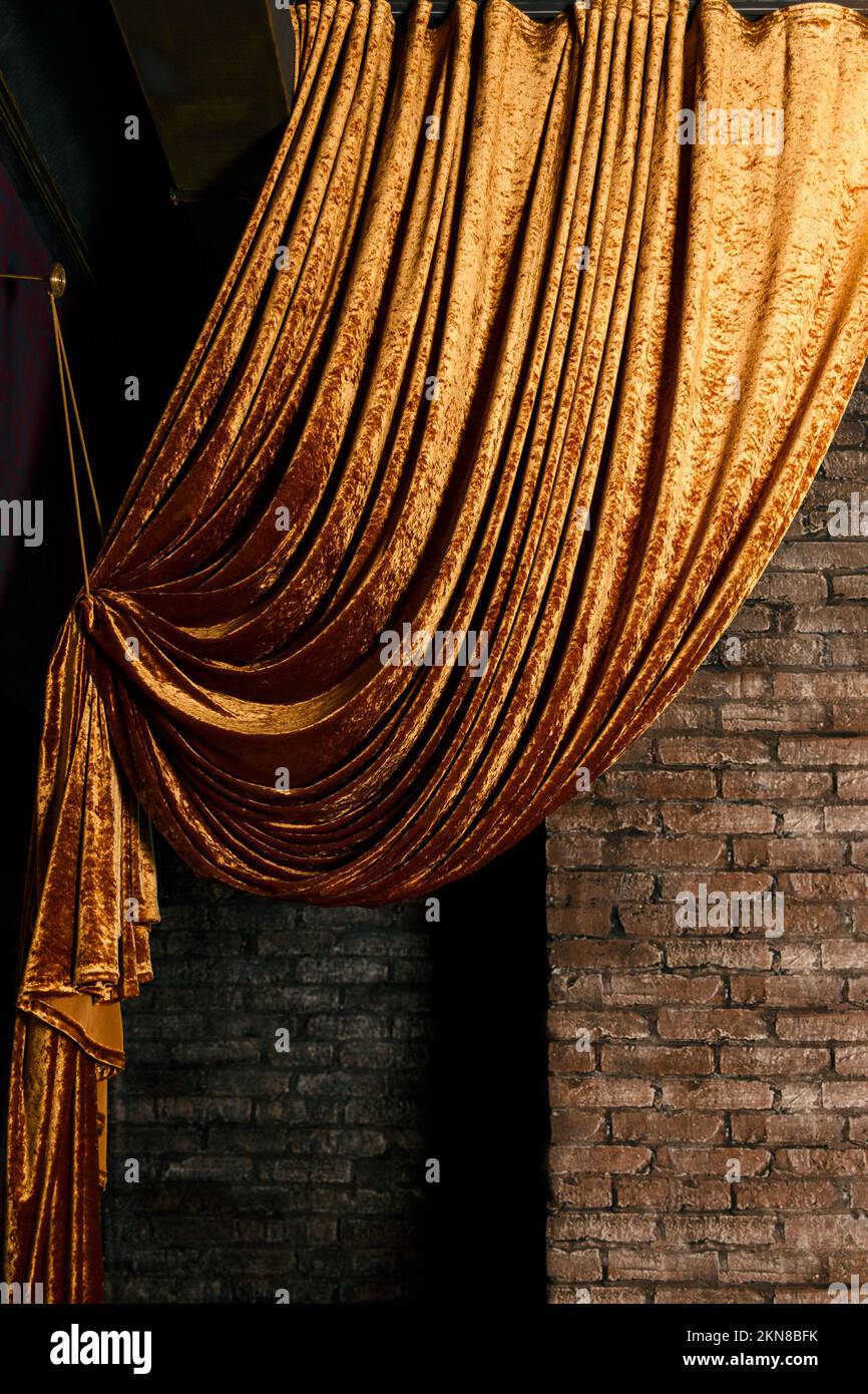 Golden big curtain on brick wall Stock Photo - Alamy