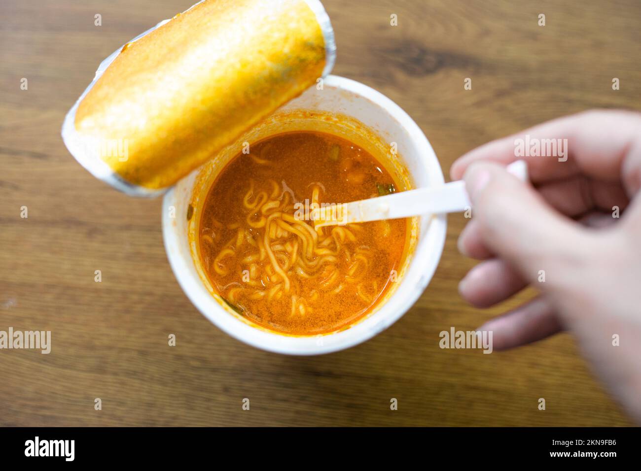 Instant noodles in a round cup are stirred with a plastic fork. Brewing ...
