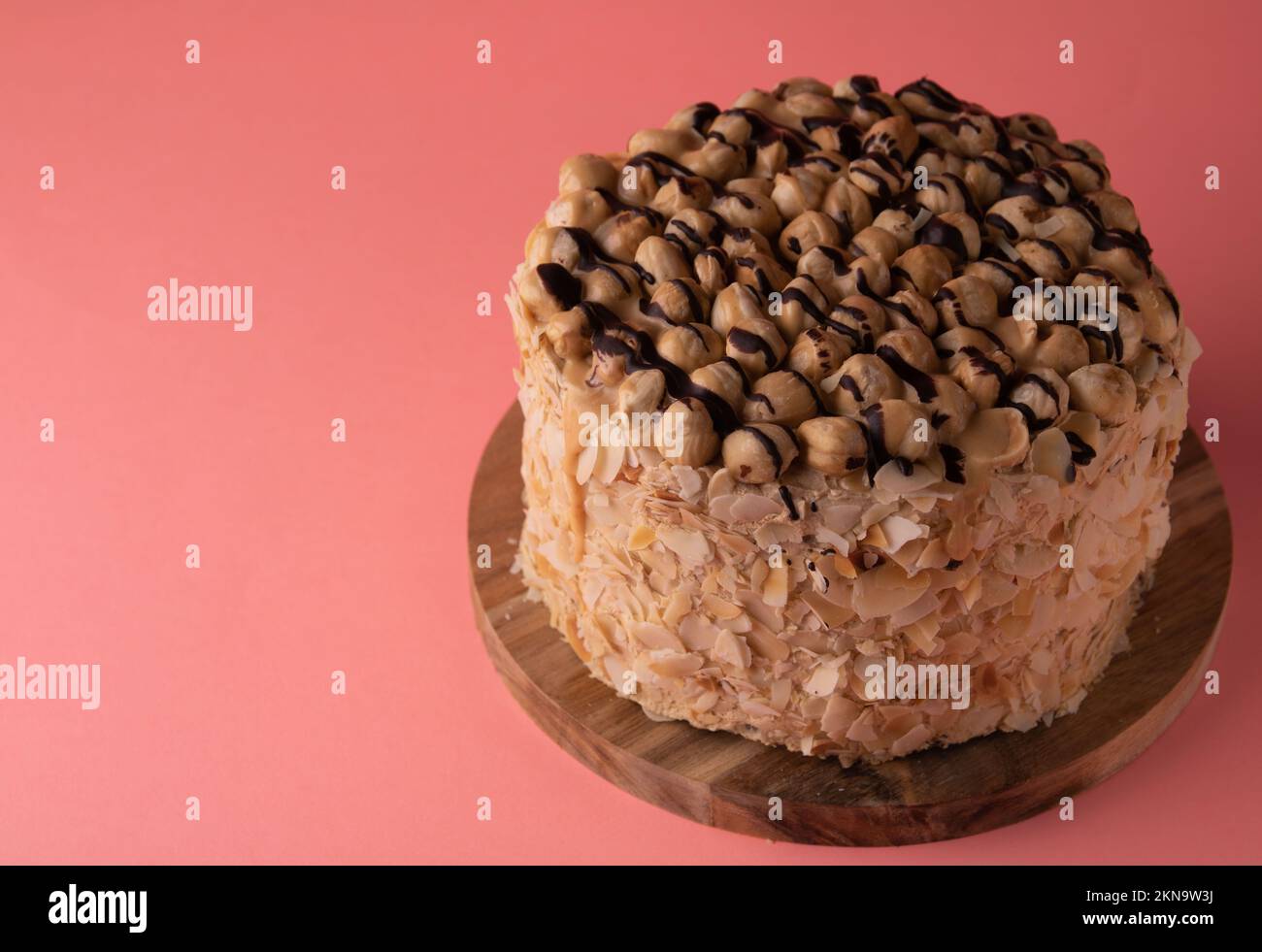 photo tall walnut cake on a wooden board stands on the side on a pink ...
