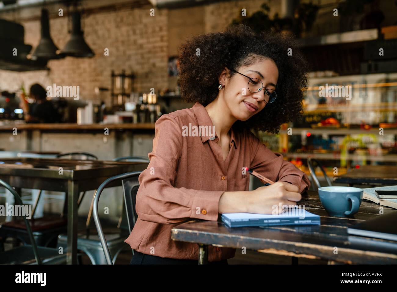 Young black woman with afro hairstyle making notes in planner book in ...