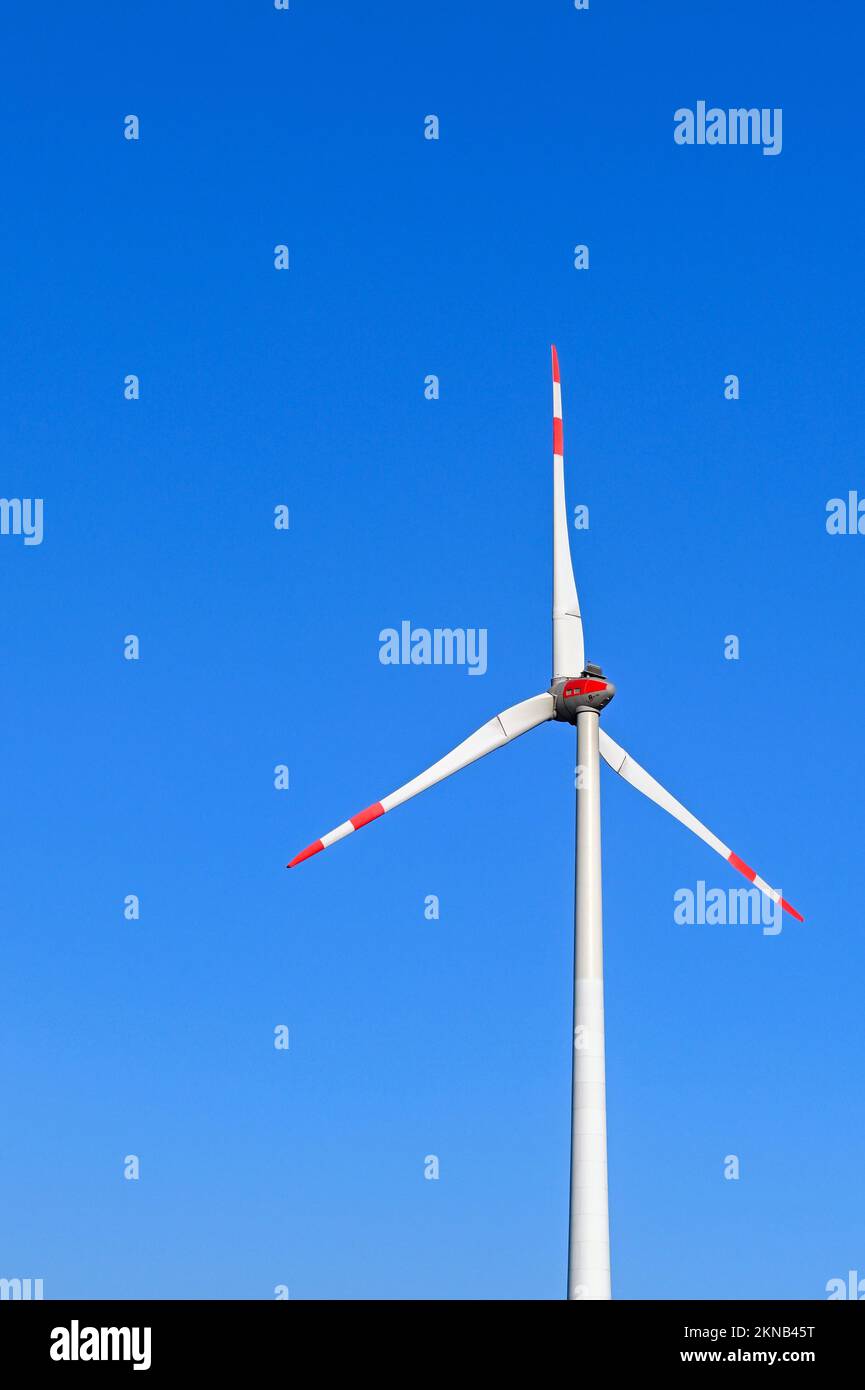 Tall wind turbine isolated against a deep blue sky. Tips of the blades ...