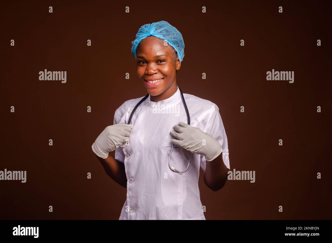 A smiling Nigerian female medic with a stethoscope isolated on a brown ...