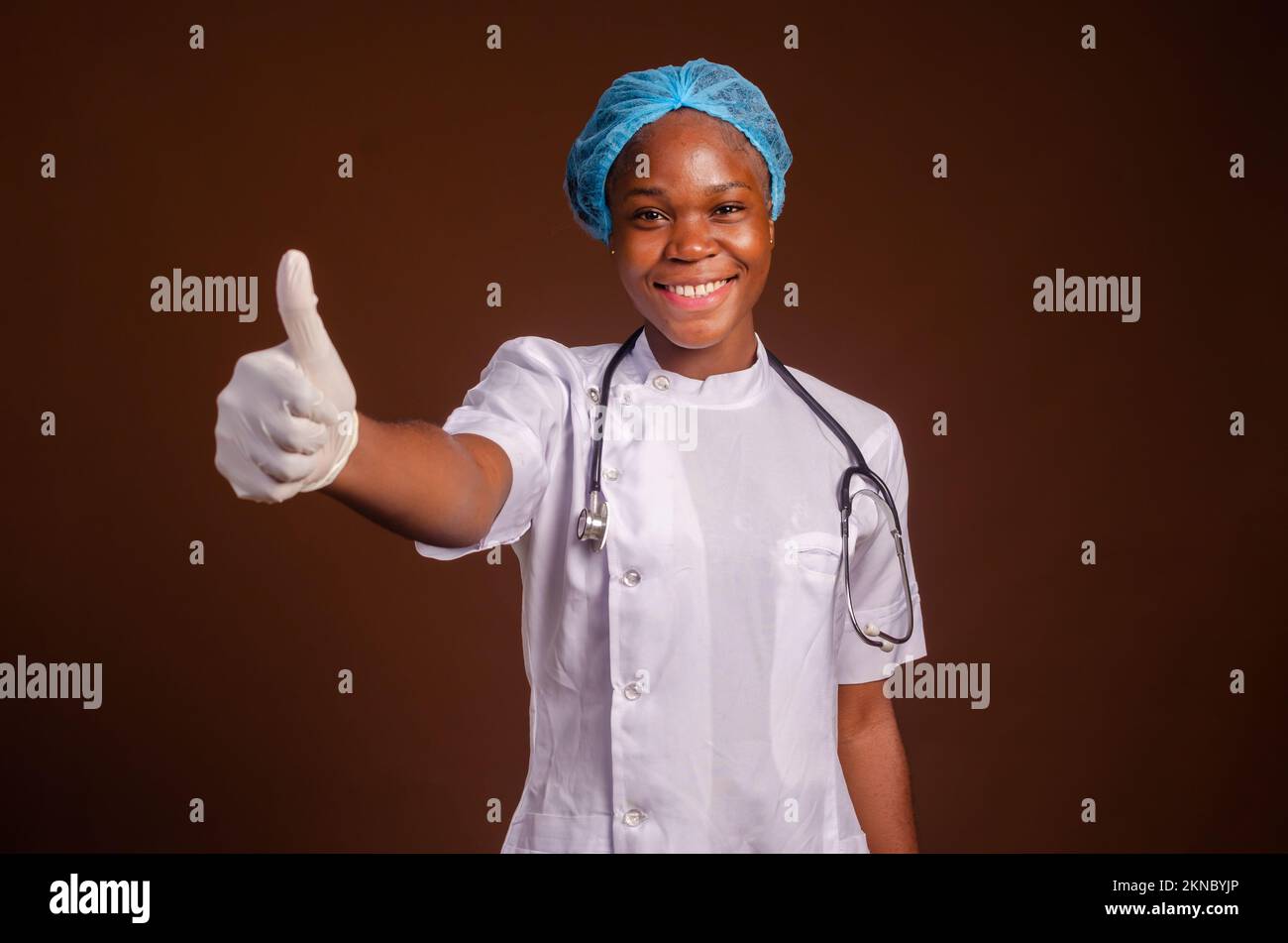 A smiling Nigerian female medic with a stethoscope showing thumb up ...