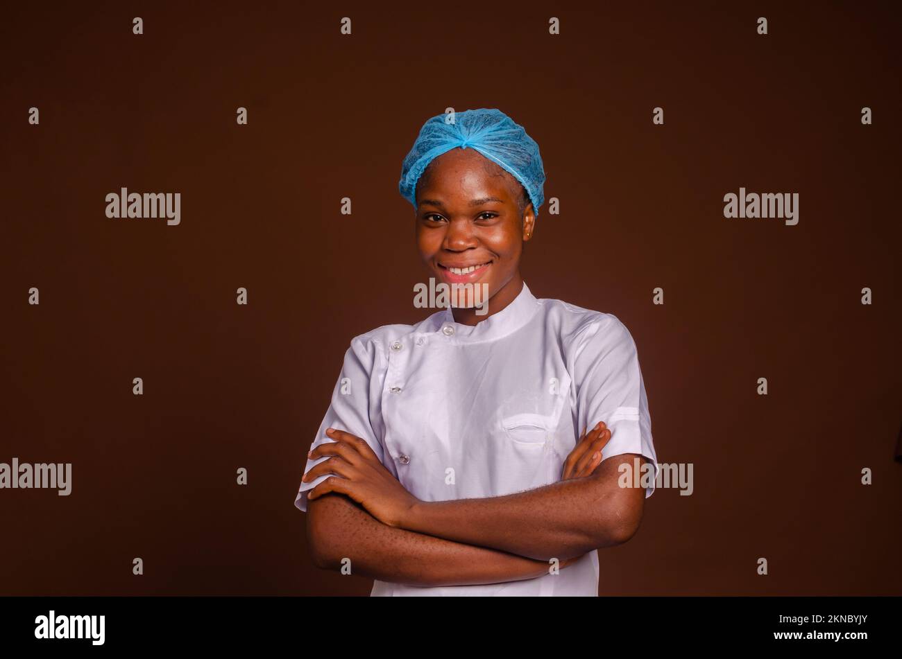 A smiling Nigerian female medic with arms crossed isolated on a brown ...