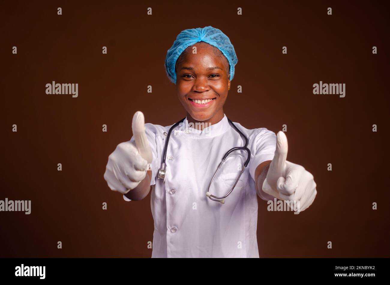 A smiling Nigerian female medic with a stethoscope showing thumb up ...