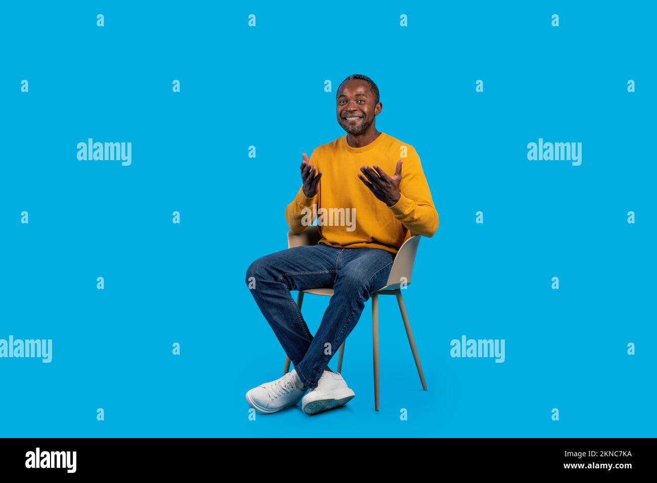 Relaxed black man sitting on chair and gesturing on blue Stock Photo ...