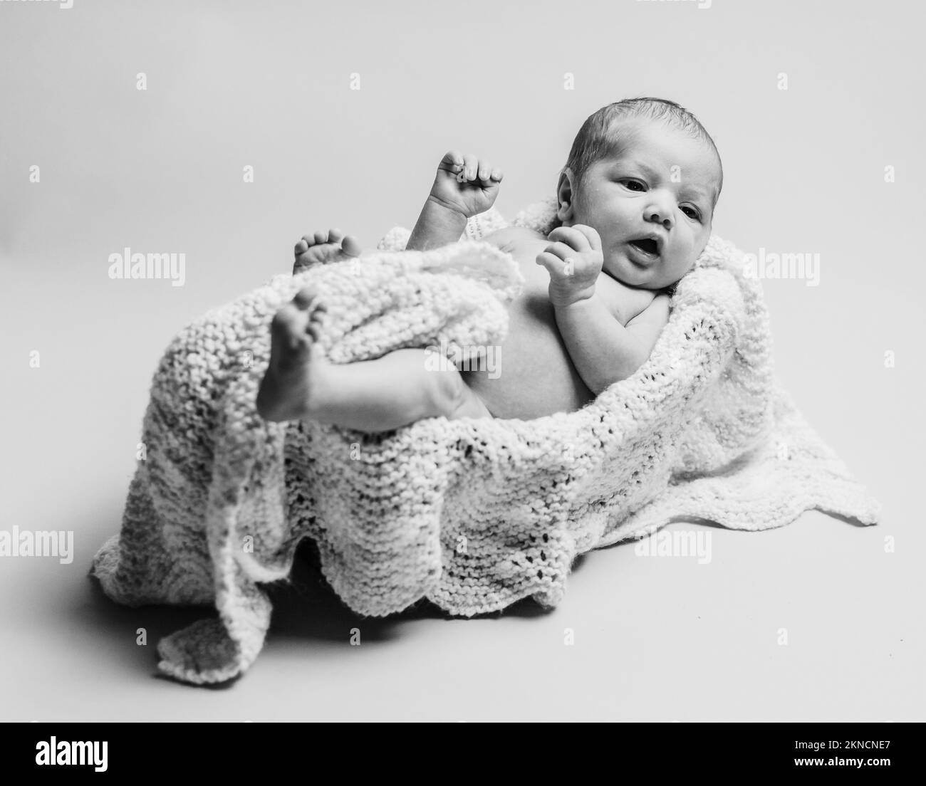 A grayscale of a newborn baby laying with a soft blanket Stock Photo ...
