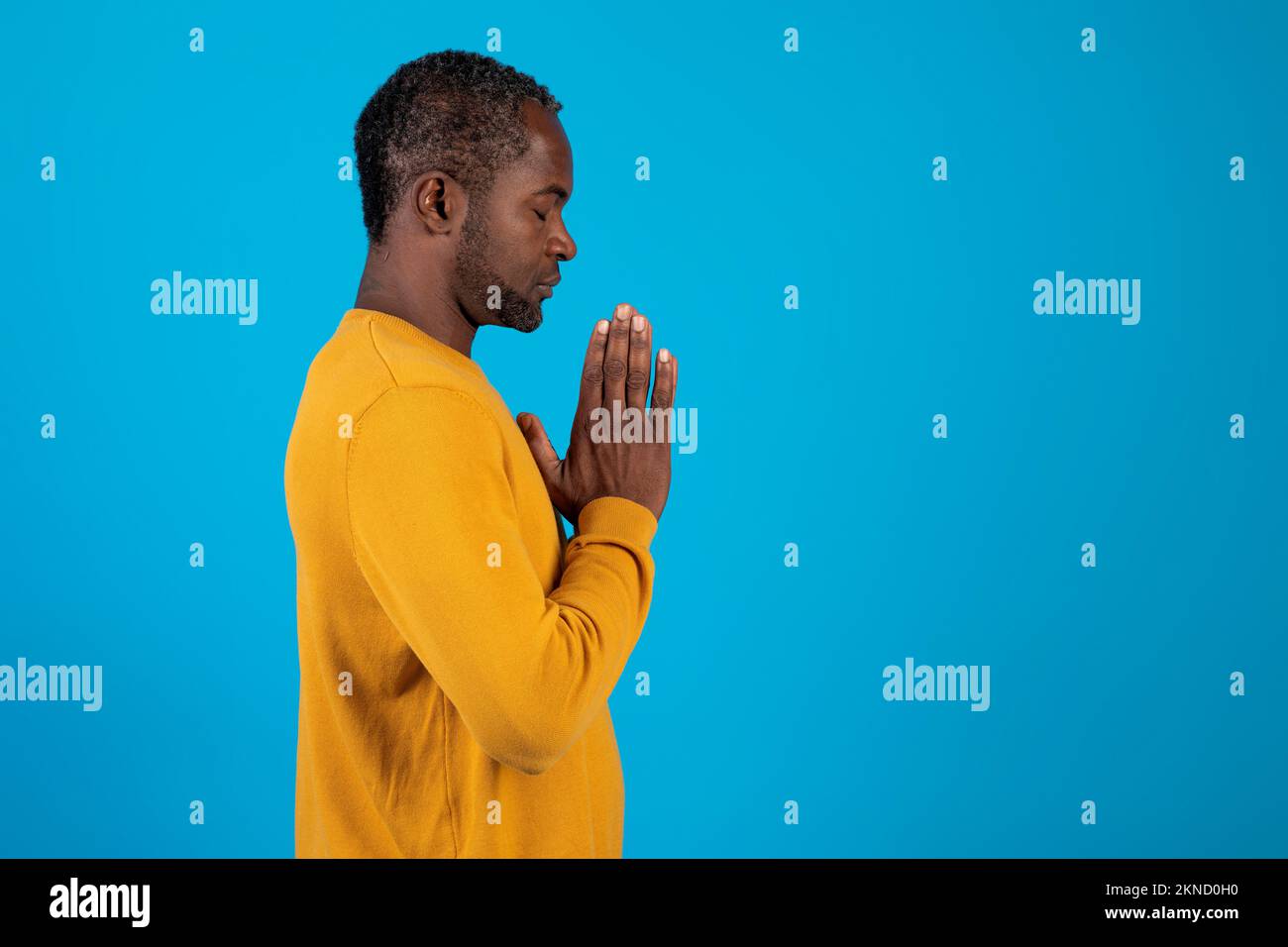 Black man praying with closed eyes on blue, side view Stock Photo - Alamy