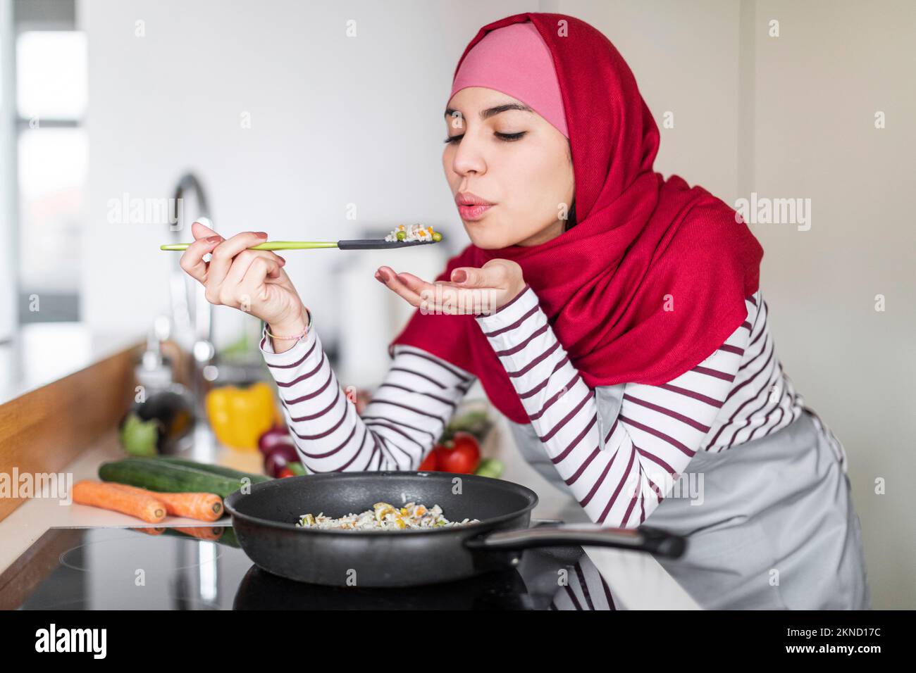 Beautiful muslim woman tasting meal while cooking Stock Photo - Alamy