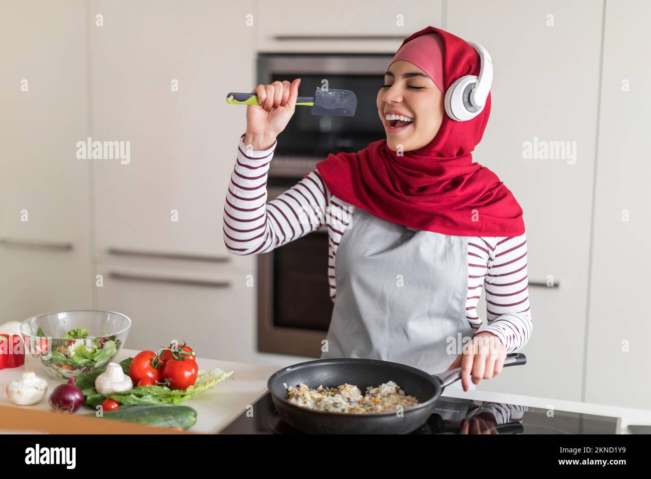 Pretty muslim woman housewife wearing hijab singing while cooking Stock ...