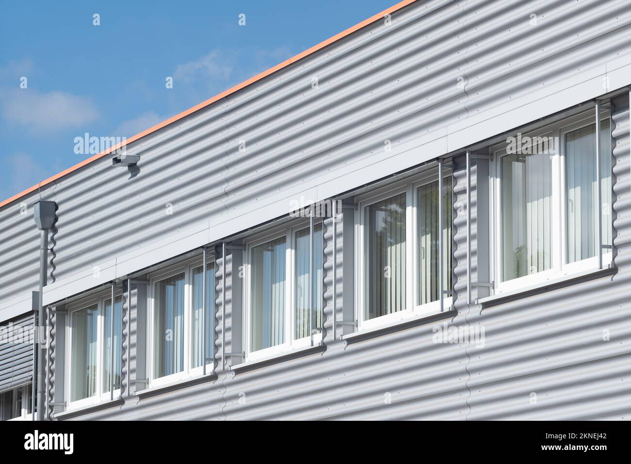 The facade of a building with glass windows against a blue cloudy sky ...