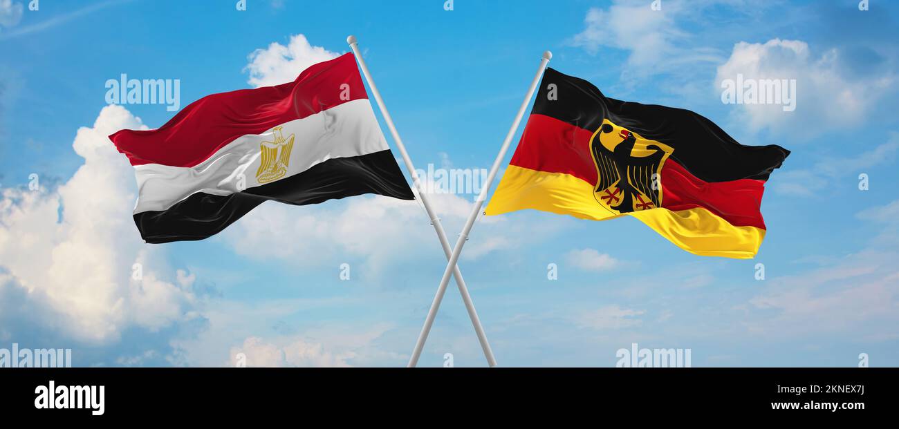 two crossed flags Germany and Egypt waving in wind at cloudy sky ...