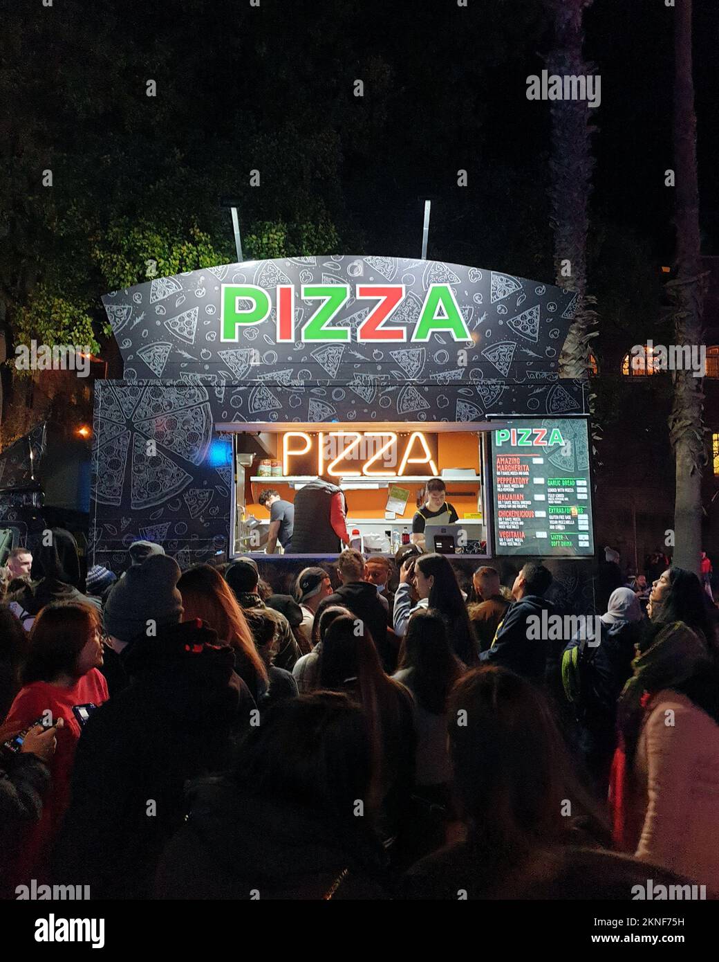 A vertical shot of a group of people standing in front of a Pizza fast ...
