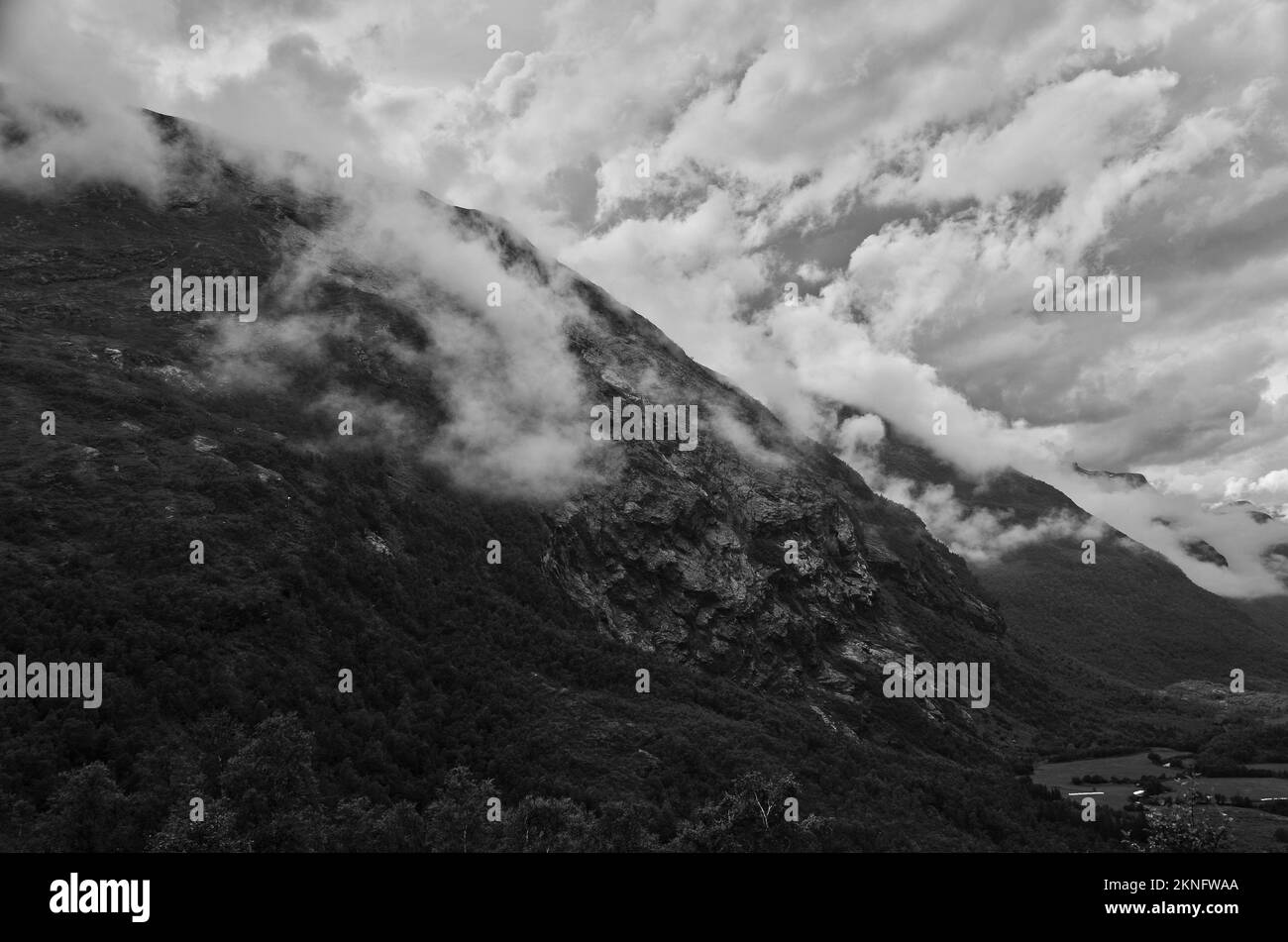 A grayscale shot of the clouds over the high forested mountains Stock ...