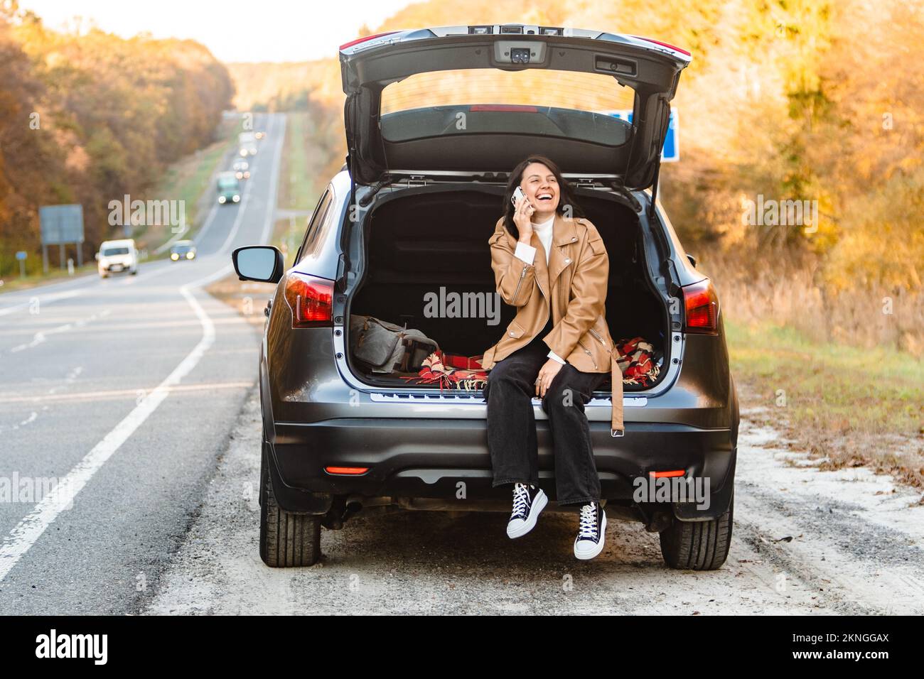 Laughing woman talking on the phone while she sits in the trunk of a ...