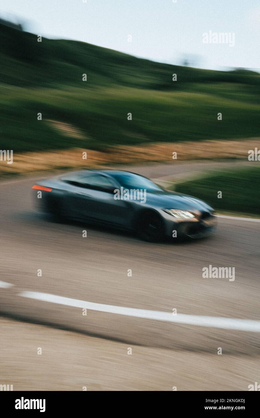 A vertical shot of a sports car speeding on a road during the daytime ...