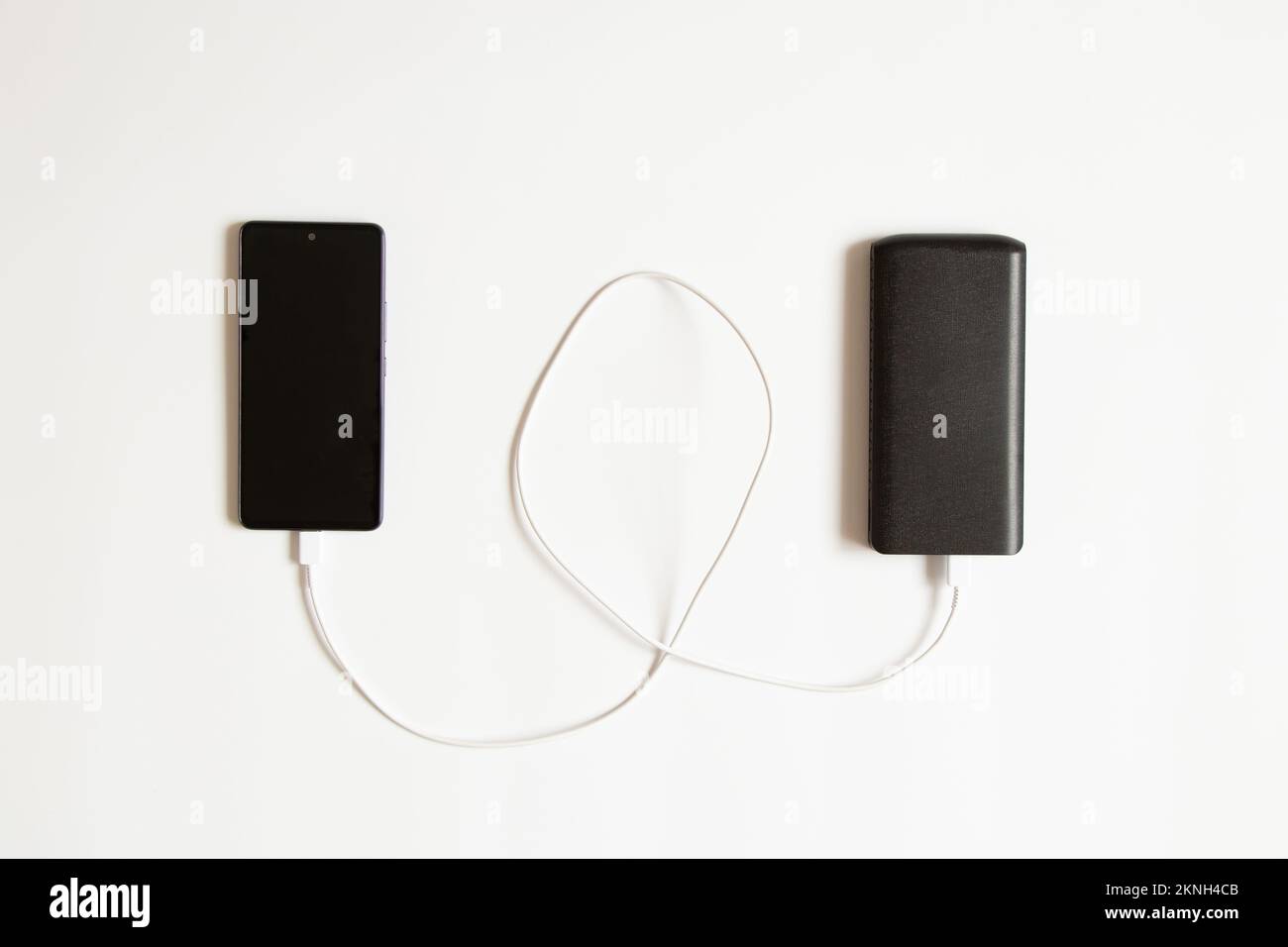 A portable rechargeable battery and a smartphone lie on a white ...