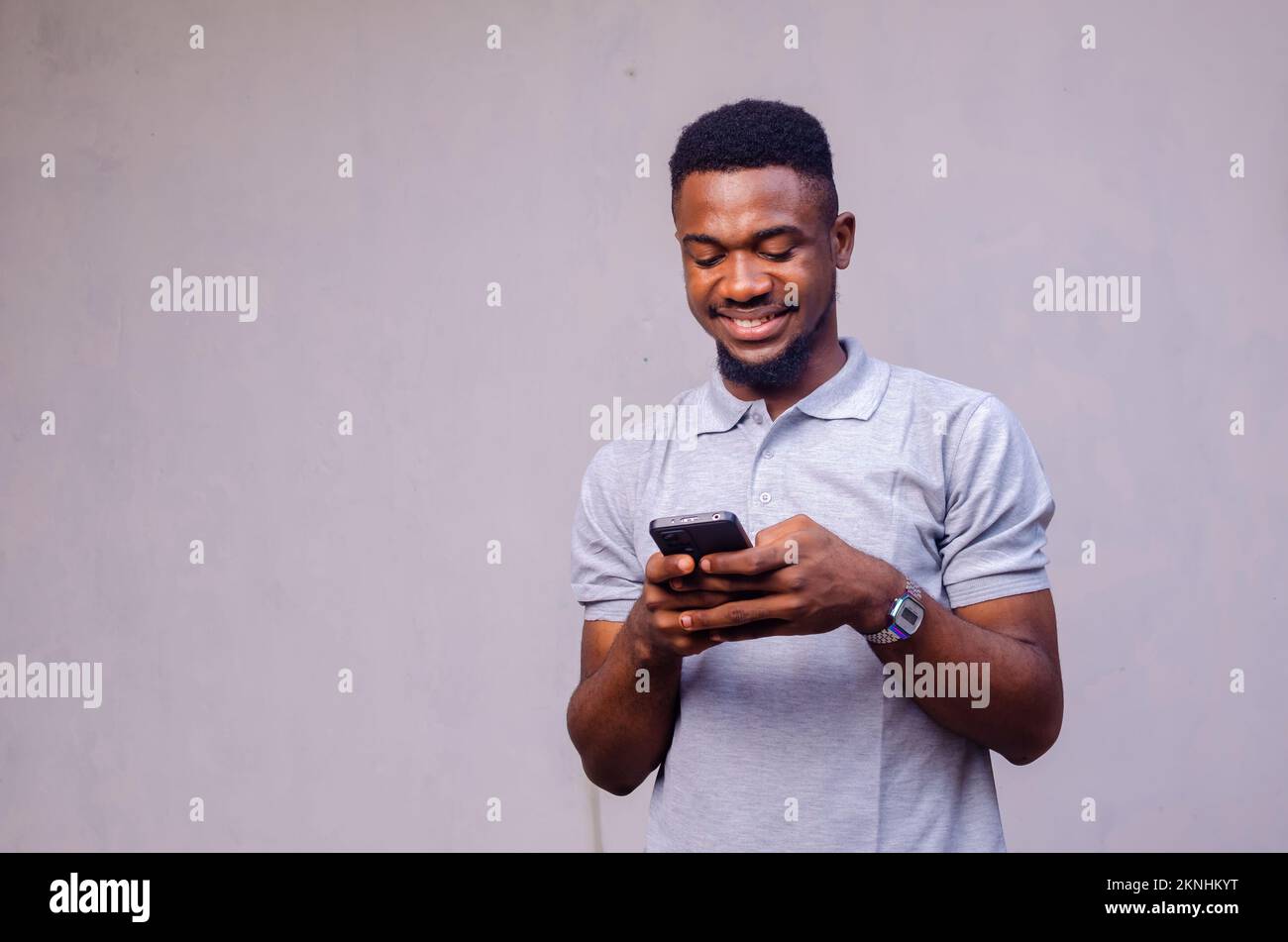 A cheerful African-American man using his phone on a grey background ...
