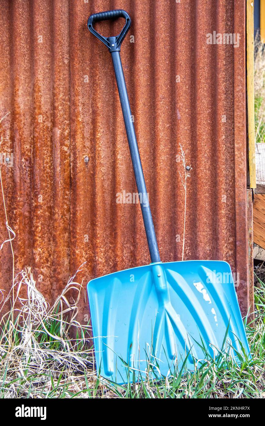 Shinny blue metal show shovel leaning against a grainy rusty corregated ...