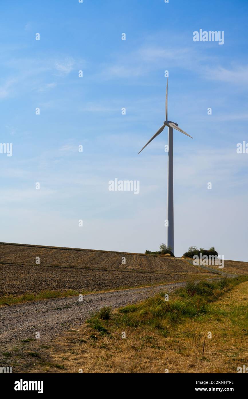 A vertical shot of tall wind turbine in the field on blue sky ...