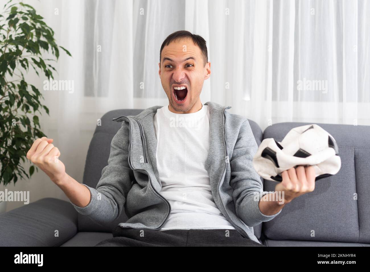 Portrait of excited young guy watching football match, raising clenched ...
