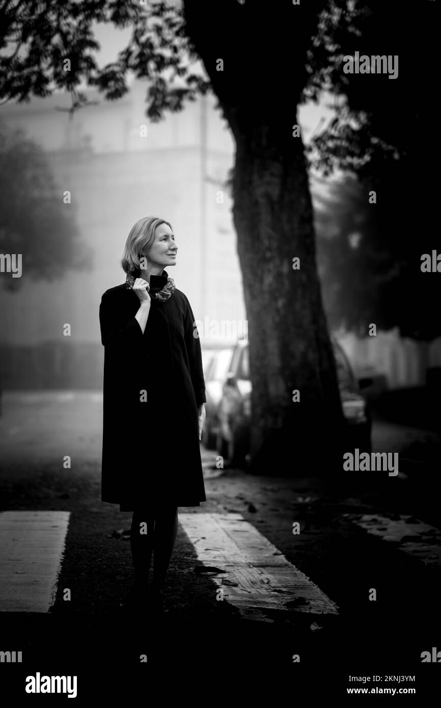 A woman stands on the sidewalk near an autumn garden. Black and white ...