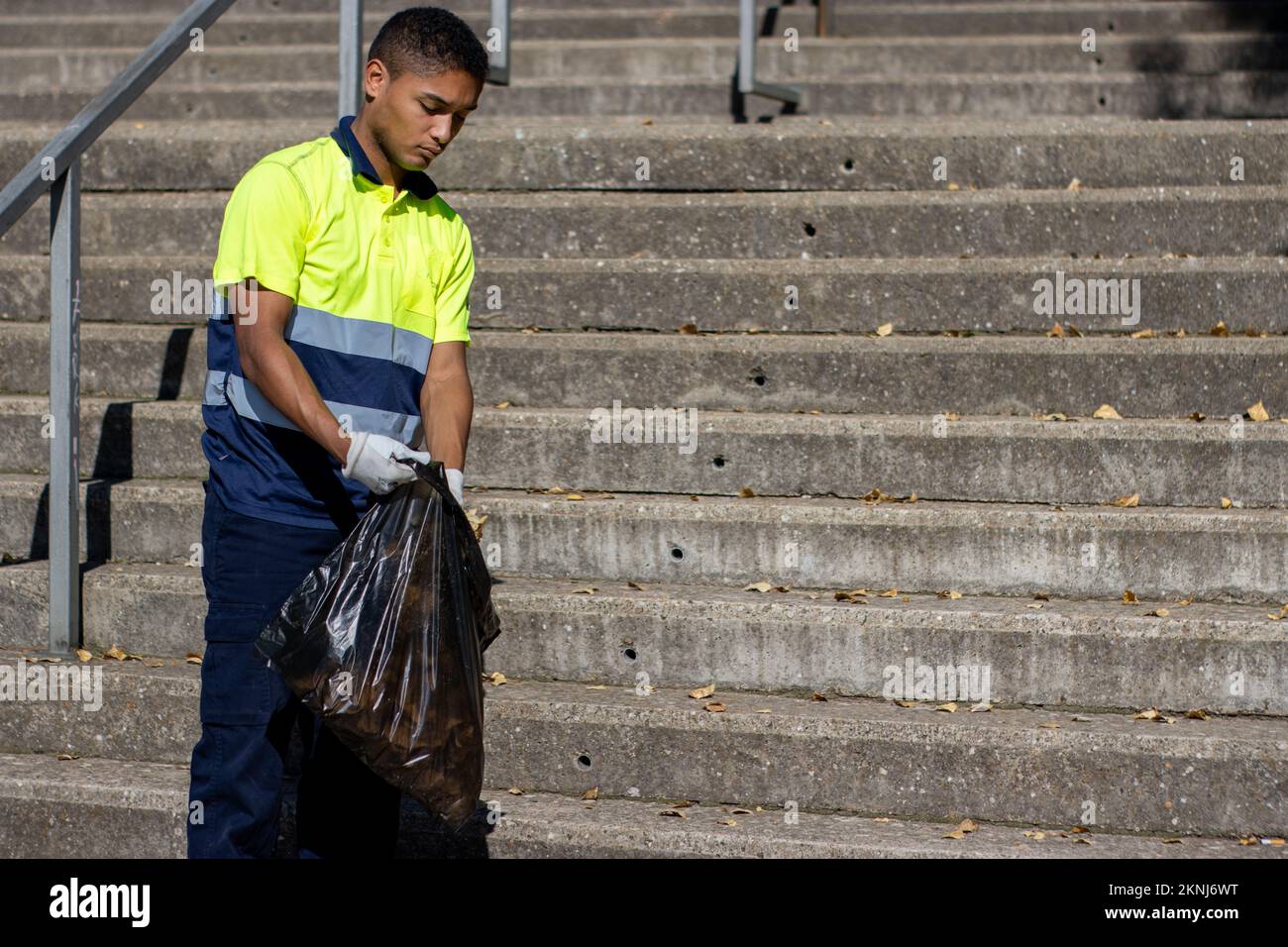 A Latino male garbage collector in work uniform collecting garbage from ...