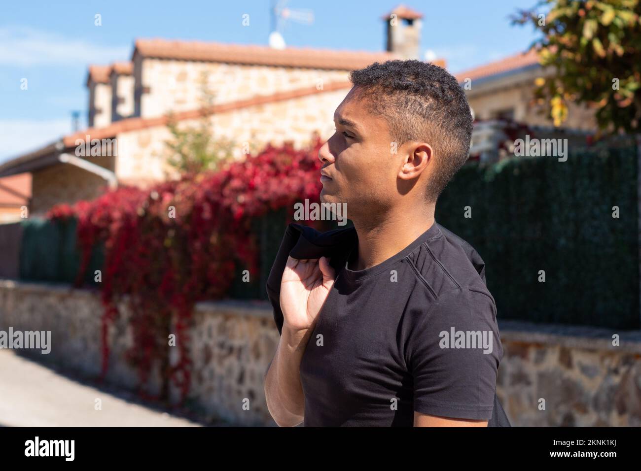 A confident young man in black with a jacket on his shoulder posing and ...