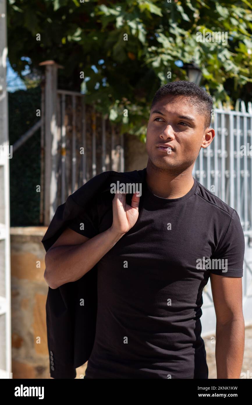 A casual young man with a black jacket on his shoulder looking away ...