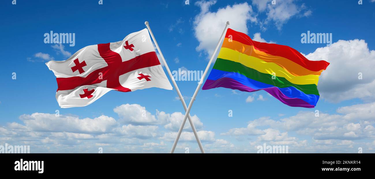 two crossed flags LGBT Pride and Georgia waving in wind at cloudy sky ...