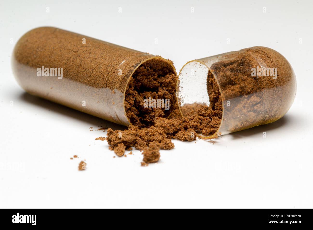 A close-up shot of an open capsule filled with brown powder medicine ...