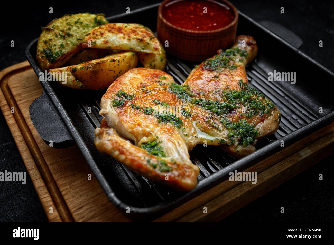 Fried half chicken with fried potatoes and spicy sauce, on a frying pan ...
