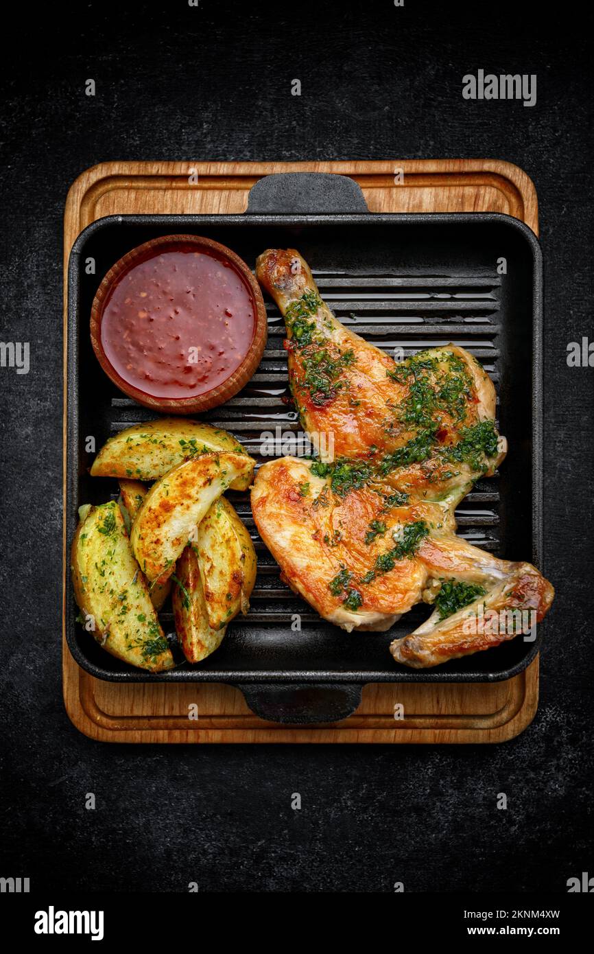 Fried half chicken with fried potatoes and spicy sauce, on a frying pan ...