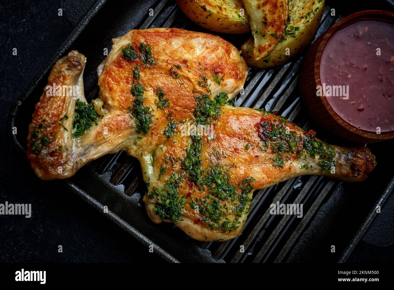 Fried half chicken with fried potatoes and spicy sauce, on a frying pan ...