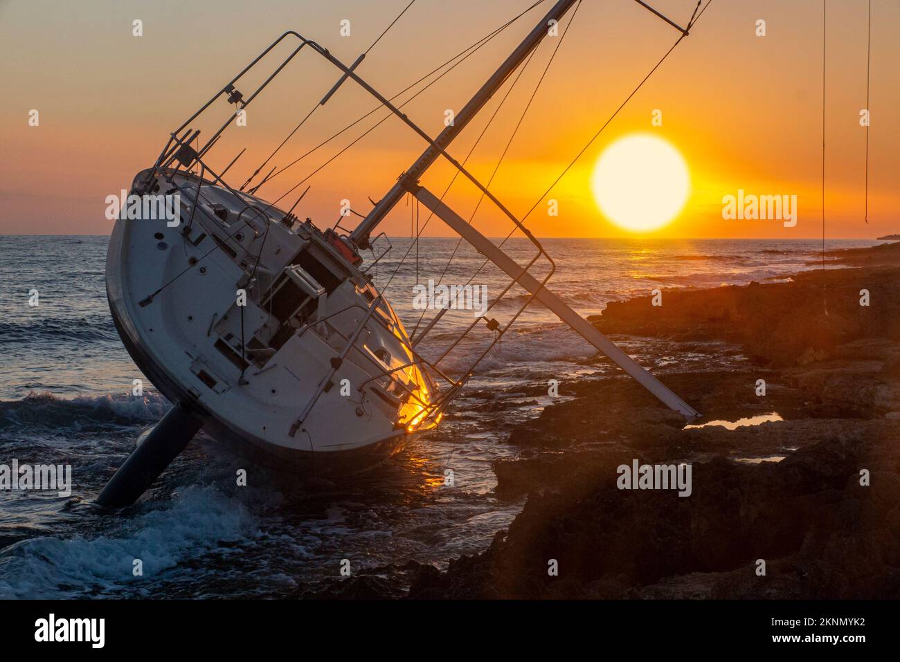 A yacht, run aground on the rocky coatd of Siciiy, Italy at sunset ...