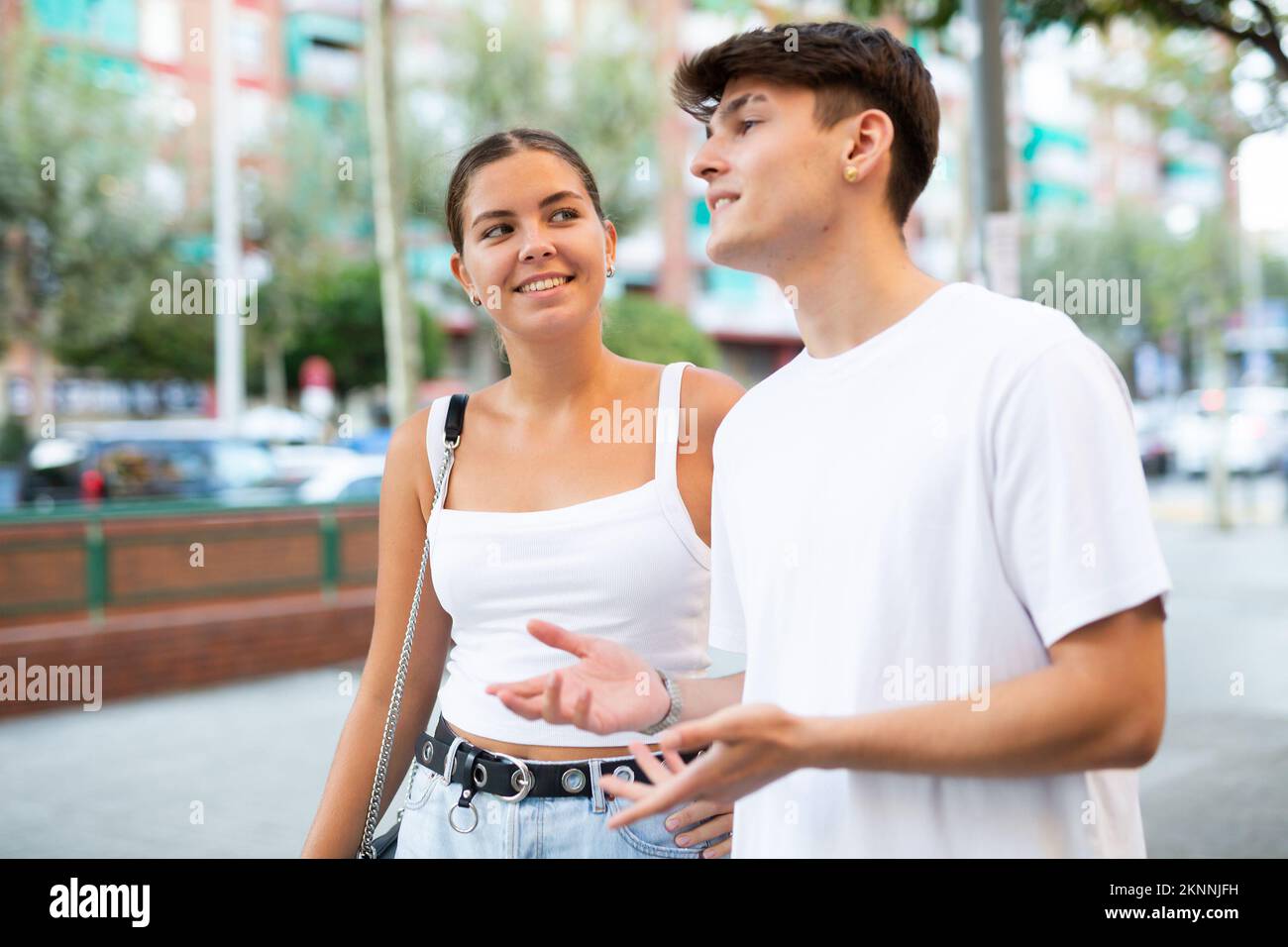 Cheerful friendly young couple walking together through summer city ...