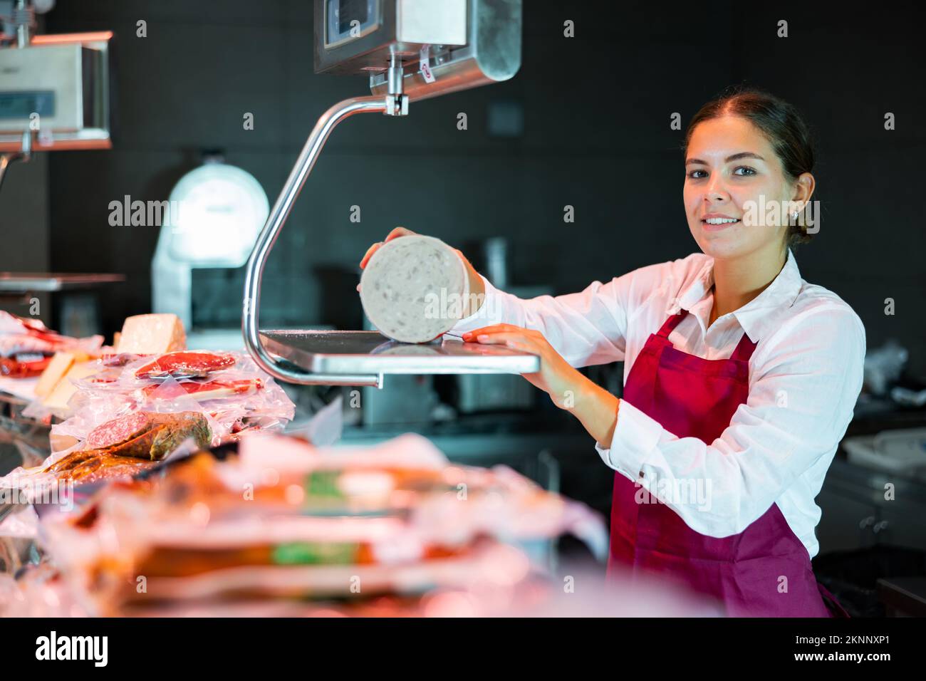 Young female seller of grocery store weighing mortadella on scales ...